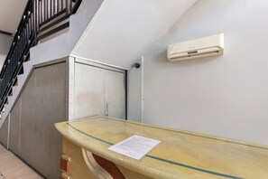 Quarto de hotel com bancada de mármore, ar condicionado branco, escada e uma porta.