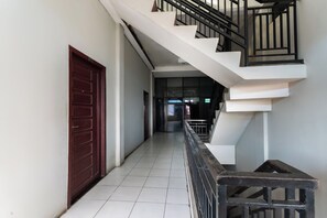Um corredor com uma porta vermelha, uma escada com grades pretas e um chão em mosaico.