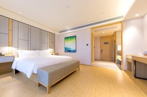 Quarto de hotel com cama, mesa de cabeceira, um banco, obra de arte e porta para o banheiro.