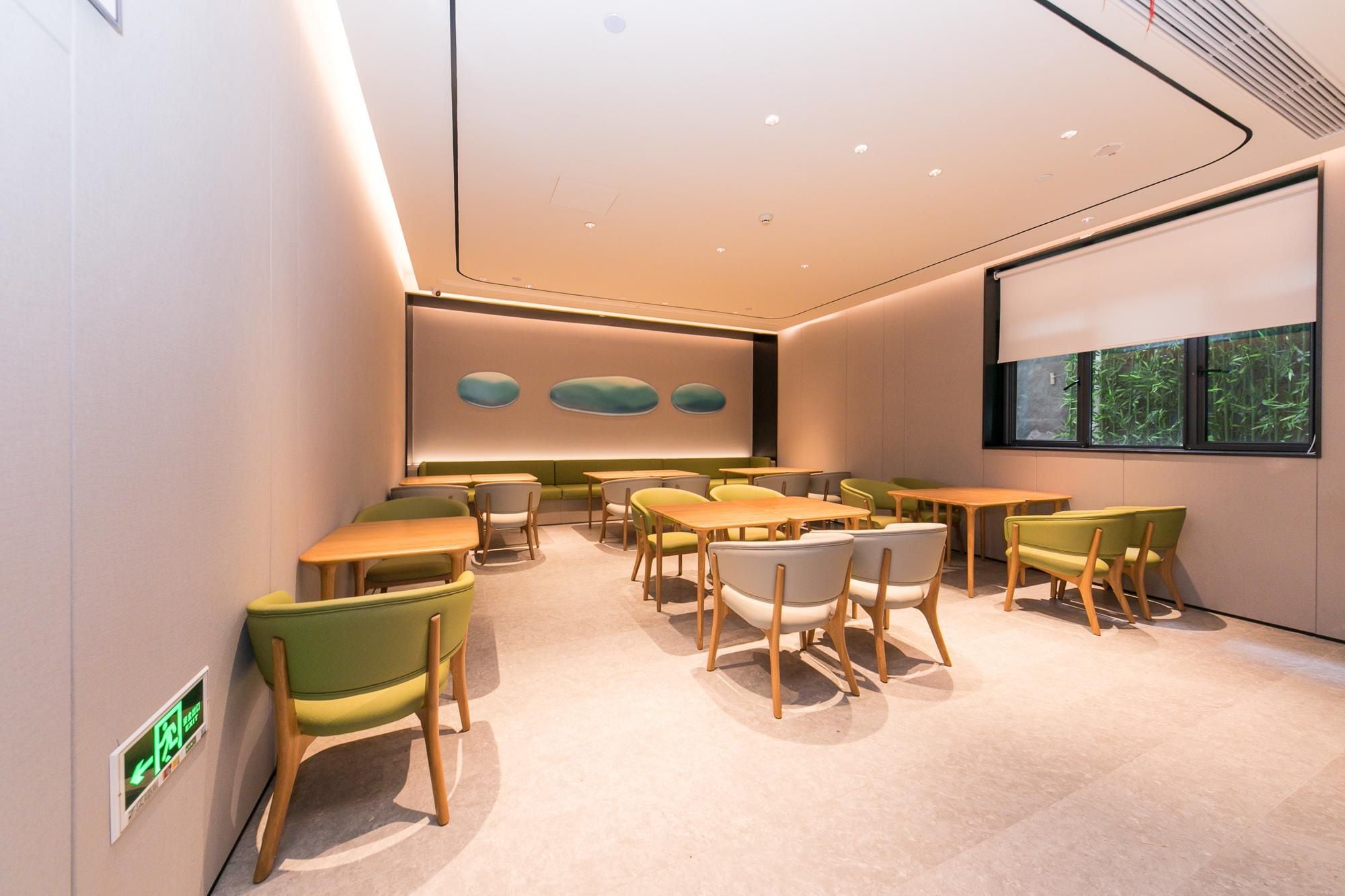 Uma sala de reuniões moderna com mesas e cadeiras, uma tela de projetor e uma janela grande com vista.