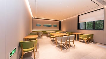 Uma sala de reuniões moderna com mesas e cadeiras, uma tela de projetor e uma janela grande com vista.