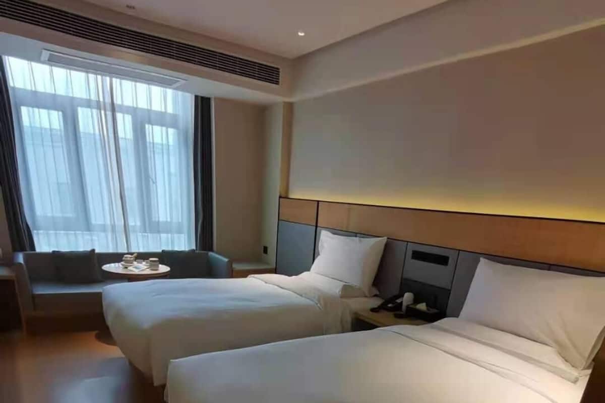 Quarto de hotel com duas camas, um sofá, uma mesa pequena e uma janela com cortinas.