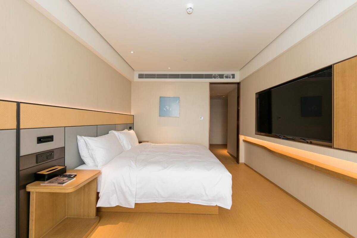 Quarto de hotel moderno com cama, mesas de cabeceira, televisão e ar condicionado.