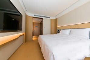 Quarto de hotel com cama grande, mesa de cabeceira, janela e porta que dá para um corredor.