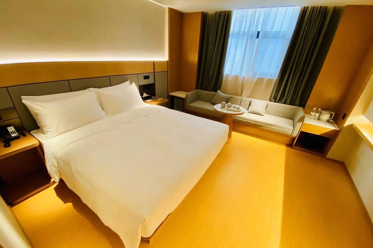 Quarto de hotel com uma cama grande, um sofá, uma mesinha com bandeja e uma mesa de cabeceira com telefone.