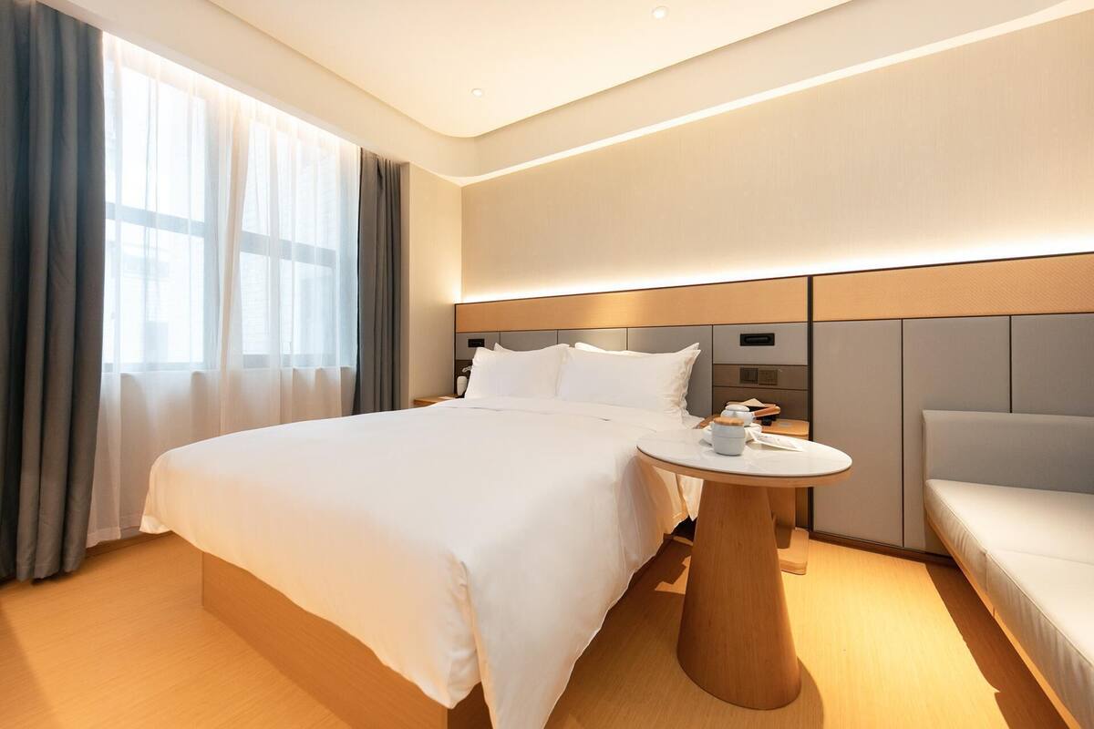 Quarto de hotel com cama grande, mesa de cabeceira e um pequeno espaço de estar.