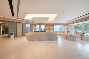 Um hall de hotel moderno com uma mesa de recepção, uma tela digital grande e vista para o exterior.
