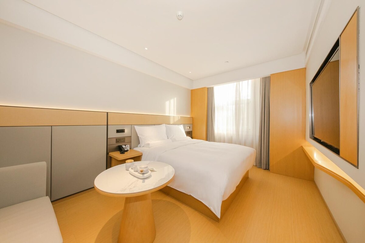 Quarto de hotel com cama, mesa de cabeceira e uma pequena mesa redonda com bandeja.