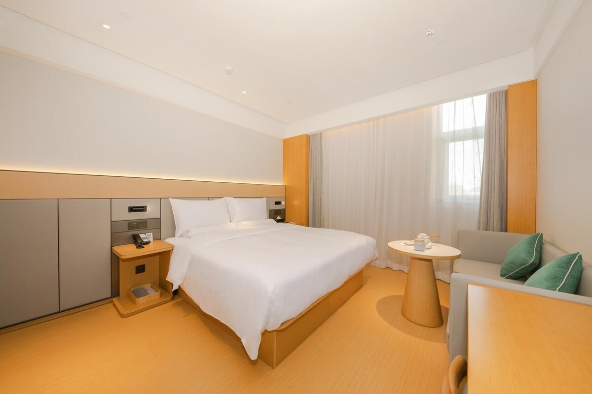 Quarto de hotel moderno com uma cama grande, mesas de cabeceira, um pequeno sofá e uma escrivaninha com cadeira.