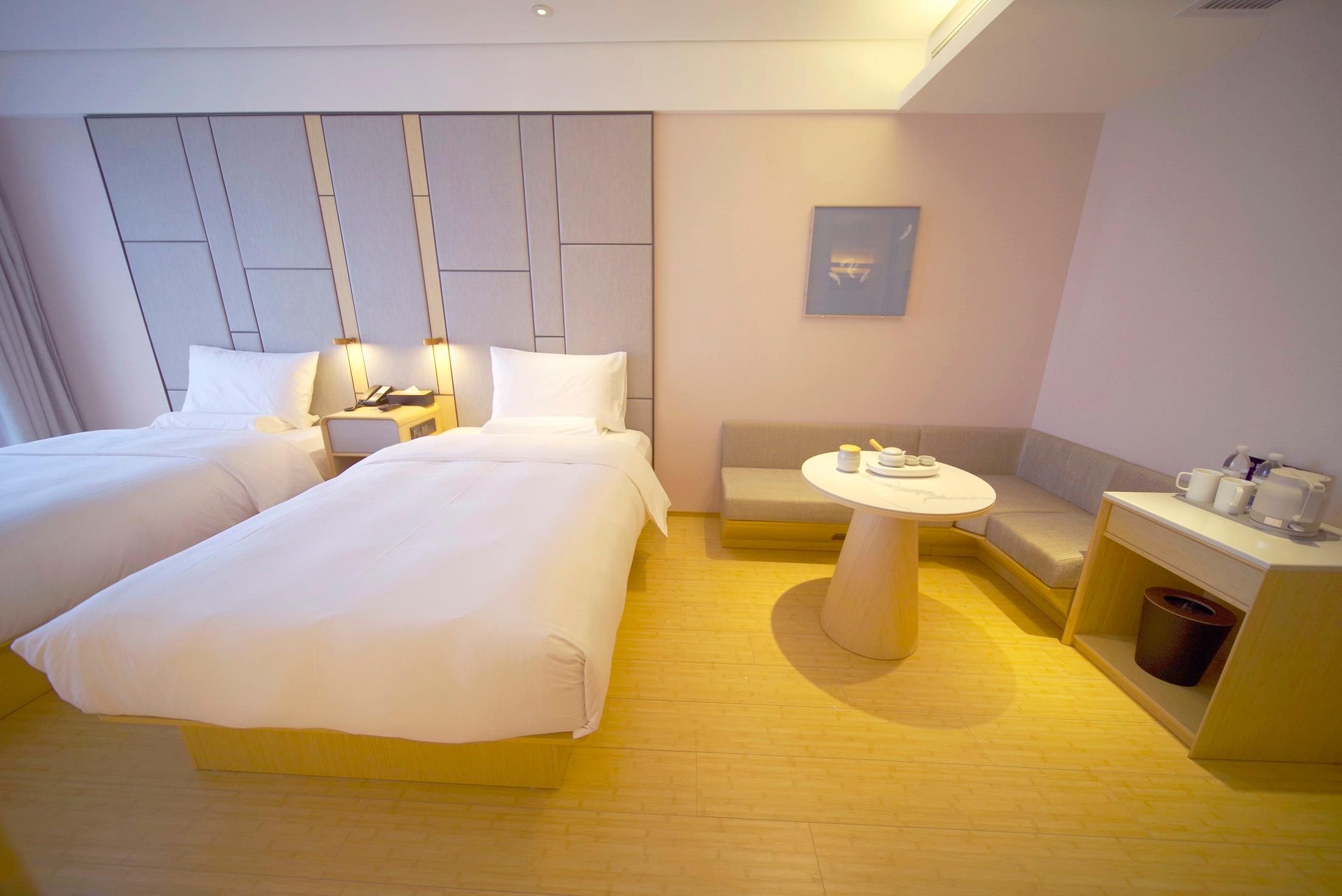 Quarto de hotel com duas camas, um sofá, uma mesa redonda pequena e uma lixeira.