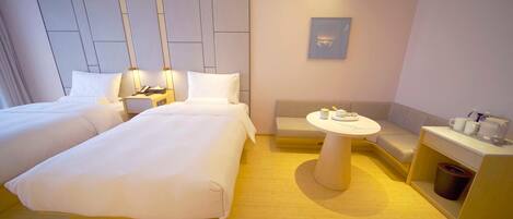 Quarto de hotel com duas camas, um sofá, uma mesa redonda pequena e uma lixeira.