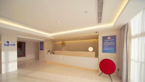 Uma área de recepção de hotel com design moderno, incluindo um balcão de atendimento, um relógio e sinalização informativa.