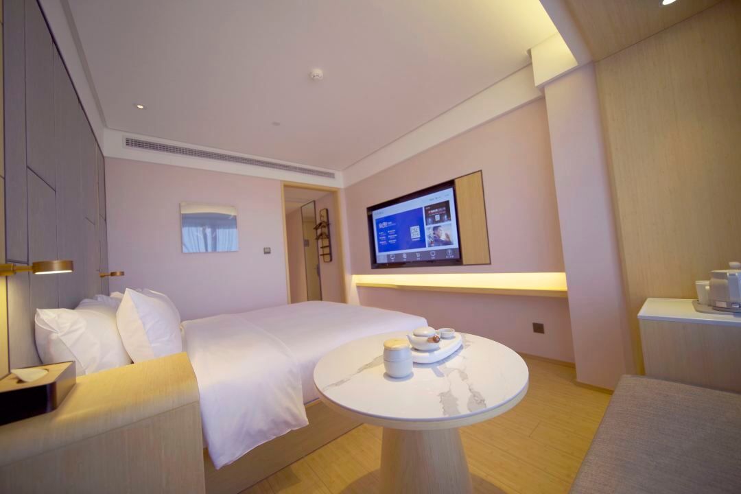 Quarto de hotel com cama, mesa redonda com um tabuleiro de objetos, televisão fixada na parede e uma pequena janela.