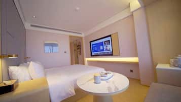 Quarto de hotel com cama, mesa redonda com um tabuleiro de objetos, televisão fixada na parede e uma pequena janela.