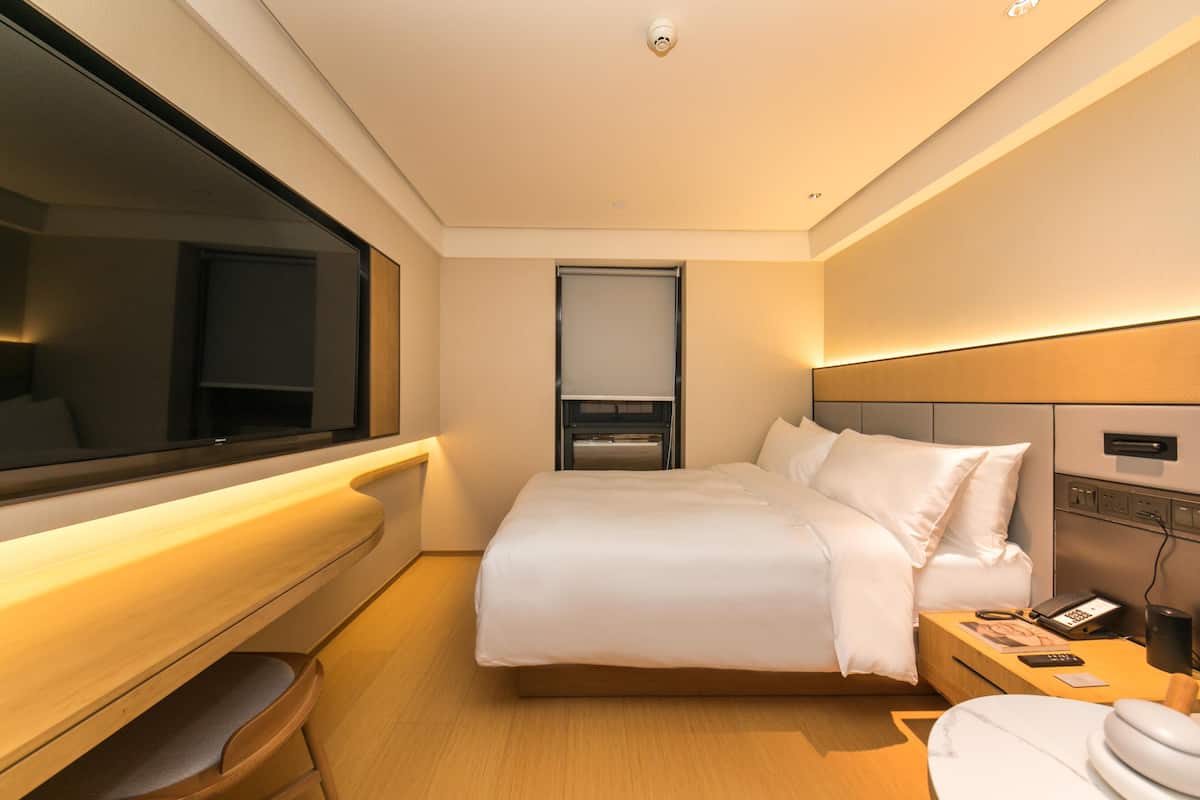 Quarto de hotel moderno com uma cama grande, mesa de cabeceira e televisão.