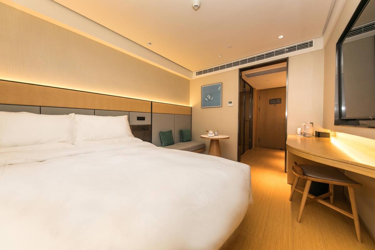 Quarto de hotel com uma cama grande, uma escrivaninha, uma cadeira, uma mesinha e uma televisão.