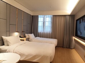 Quarto de hotel com duas camas, uma mesa de cabeceira, televisão e uma janela grande com cortinas.