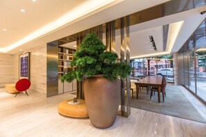 Um interior moderno com uma planta grande em vaso, uma cadeira vermelha e um espaço de refeições com mesas e cadeiras.