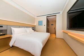 Quarto de hotel com cama, mesas de cabeceira, televisão fixada na parede e porta que dá para outro quarto.