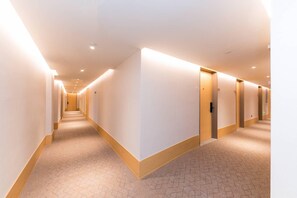 Um corredor longo e bem iluminado, com carpetes e portas ao longo de um lado.