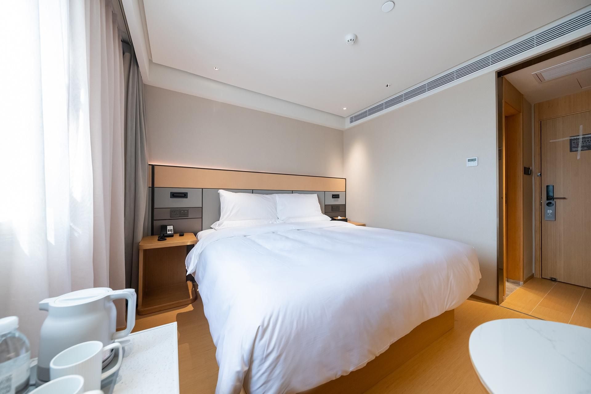 Quarto de hotel com uma cama, mesa de cabeceira e uma pequena mesa com chá e chaleira.