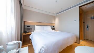 Quarto de hotel com uma cama, mesa de cabeceira e uma pequena mesa com chá e chaleira.