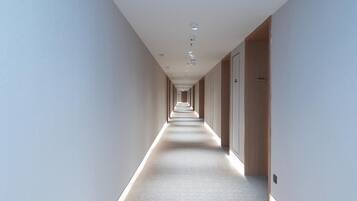 Um corredor comprido e estreito com piso coberto por carpete, iluminação embutida e portas em ambos os lados.
