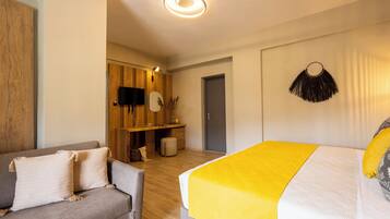 Quarto de hotel moderno com cama, sofá, escrivaninha e televisão.