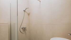 Casa de banho com cabine de chuveiro em vidro, lavatório branco e azulejos bege.