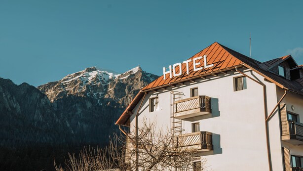 Um hotel com uma placa identificando 'HOTEL' no telhado, com montanhas ao fundo.