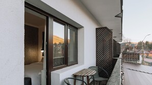 Uma varanda com mesa e cadeiras, uma janela com vista para um edifício e uma parede decorativa.