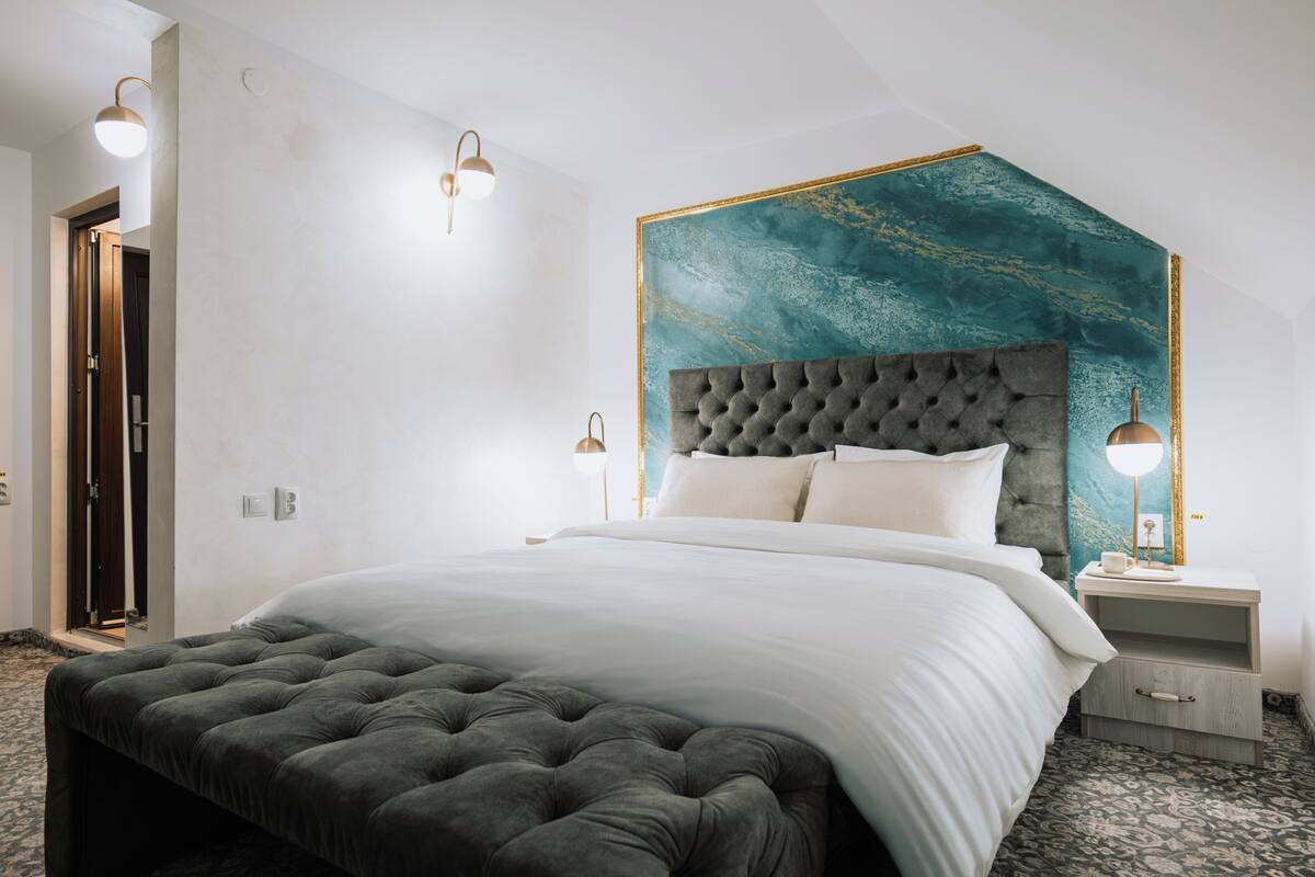 Quarto com cabeceira estofada, cama grande, mesas de cabeceira e luminária fixada na parede.
