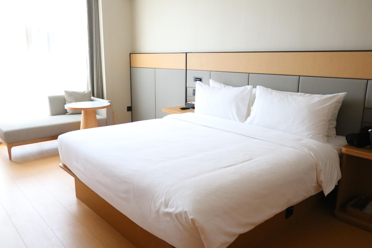 Quarto de hotel com uma cama grande, uma mesa redonda pequena, um sofá e uma mesinha de cabeceira.