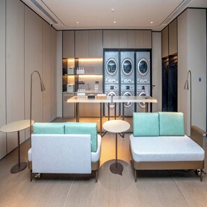 Quarto de hotel moderno com cozinha compacta, sofás, mesa e m áquina de lavar.