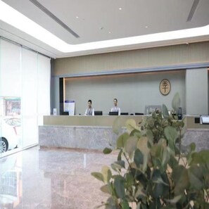 Balcão de recepção com dois funcionários, uma placa na parede com caracteres chineses e entrada por porta de vidro.