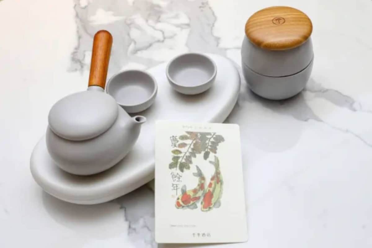 Um conjunto de utensílios de chá de cerâmica branca, incluindo um bule, xícaras e um pequeno recipiente, sobre uma superfície de mármore.