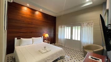 Quarto de hotel com uma cama grande, uma escrivaninha, uma cadeira, uma televisão e uma janela com cortinas.
