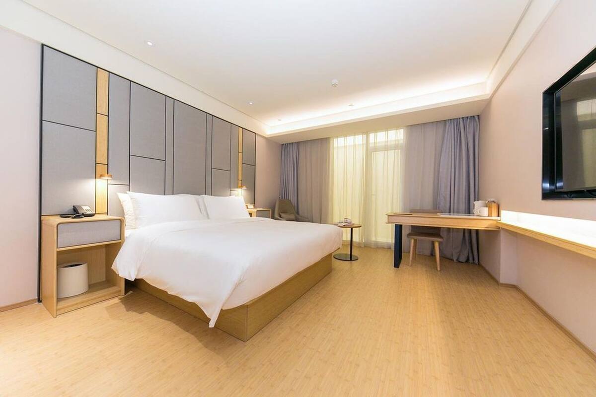 Quarto de hotel moderno com uma cama grande, mesas de cabeceira, escrivaninha e televisão.