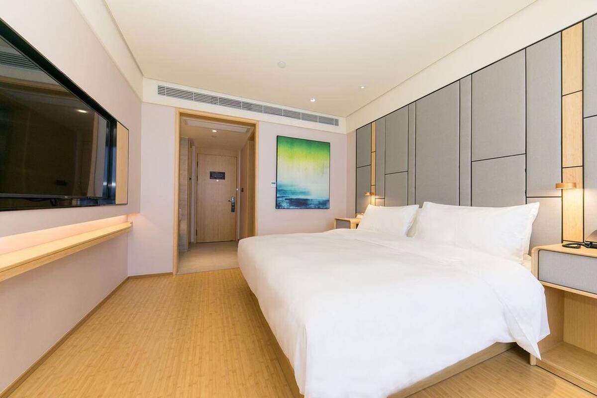 Quarto de hotel com uma cama grande, televisão de tela plana, um quadro na parede e piso de madeira.