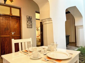 Uma mesa de jantar posta com pratos, copos e talheres, uma cadeira e uma porta de madeira com um sinal de número.