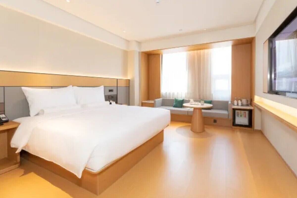 Quarto de hotel moderno com uma cama grande, um pequeno espaço para sentar e uma janela com cortinas.