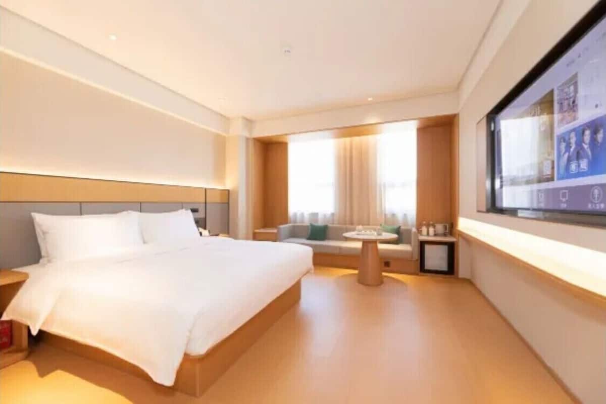 Quarto de hotel moderno com uma cama grande, um pequeno espaço de estar, uma televisão e uma janela com cortinas.