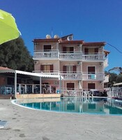 Um edifício com várias andares, varandas, piscina e área coberta com cadeiras.