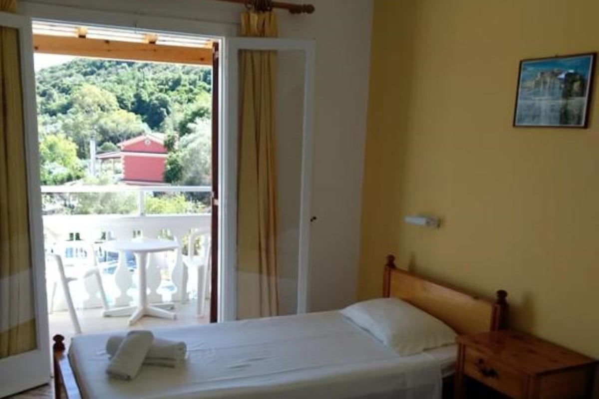 Quarto de hotel com duas camas, cabeceira de madeira, mesa de cabeceira pequena e vista para o verde através de uma porta aberta.