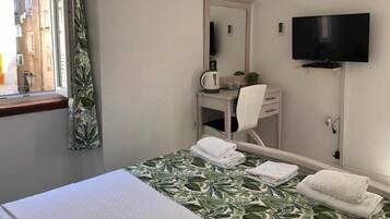 Quarto de hotel com cama, escrivaninha com cadeira, televisão e janela com cortinas.