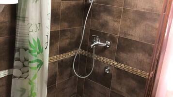Área de chuveiro com chuveiro, pulverizador de mão e torneira fixada na parede.