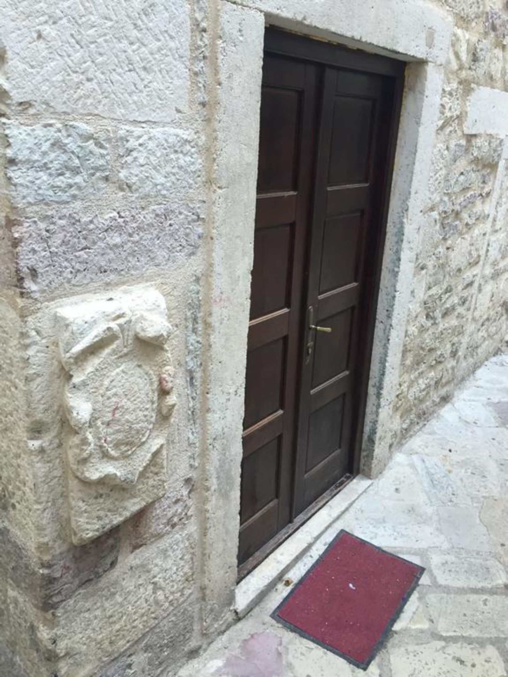 Um edifício de pedra com uma porta de madeira escura e um tapete vermelho pequeno na entrada.