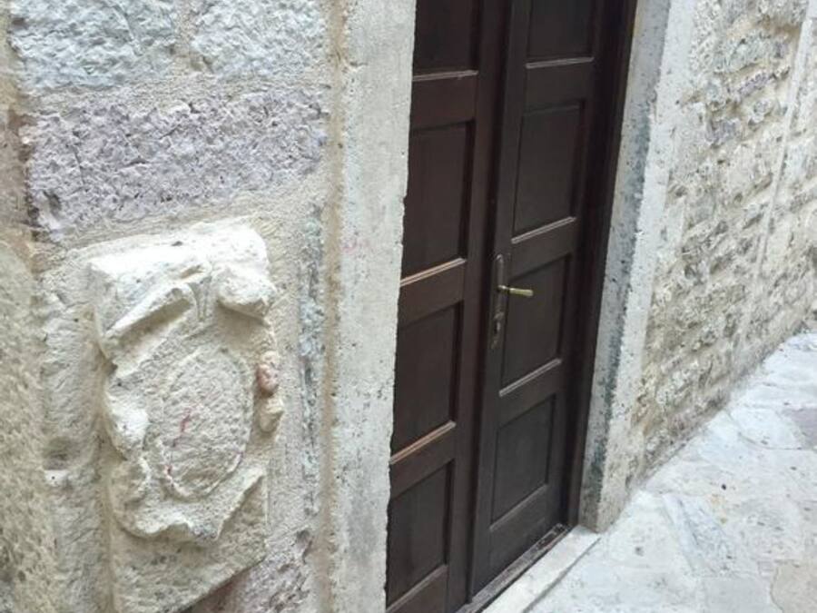 Um edifício de pedra com uma porta de madeira escura e um tapete vermelho pequeno na entrada.