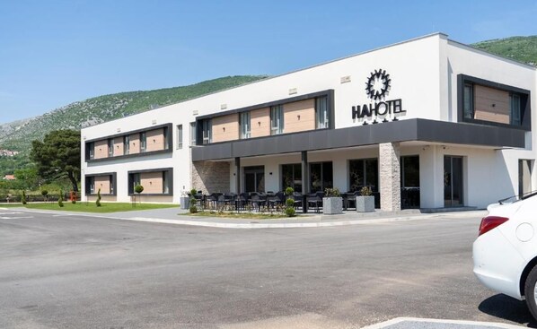 Um hotel moderno com telhado plano, logotipo em destaque e área de estar externa coberta.