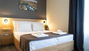 Quarto de hotel com cama, duas mesas de cabeceira, um quadro na parede e uma janela com cortinas.